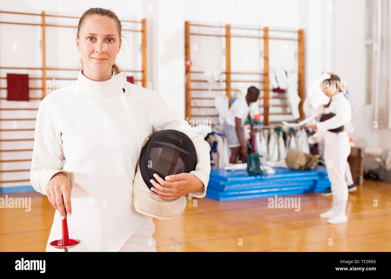 Smiling sporty young woman in uniform standing at fencing workout Stock ...