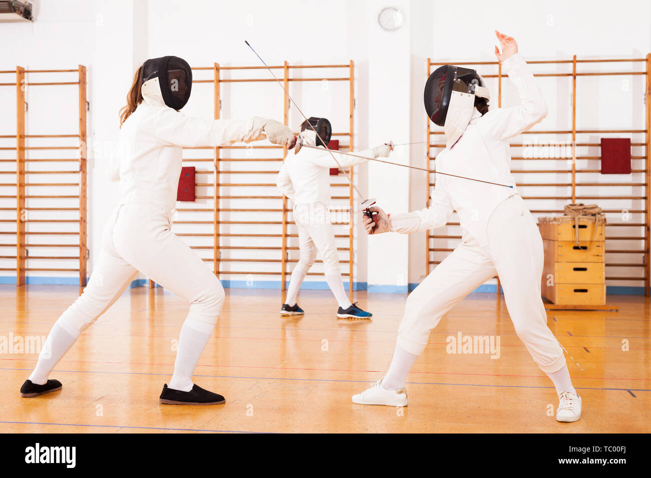 active female athletes in uniform practicing movements at fencing ...