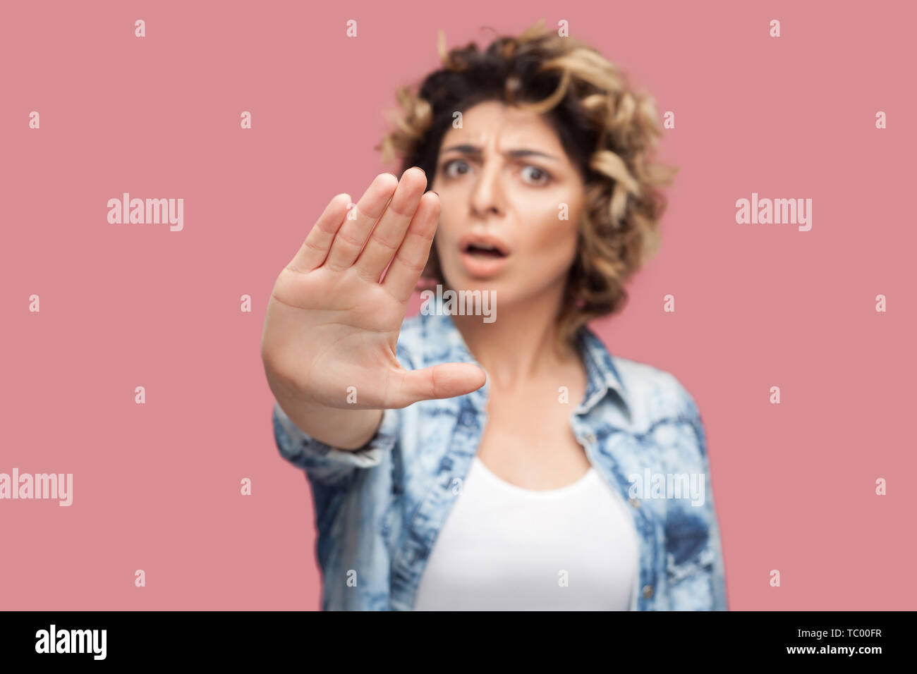 Stop. Portrait of angry young woman with curly hairstyle in casual blue ...