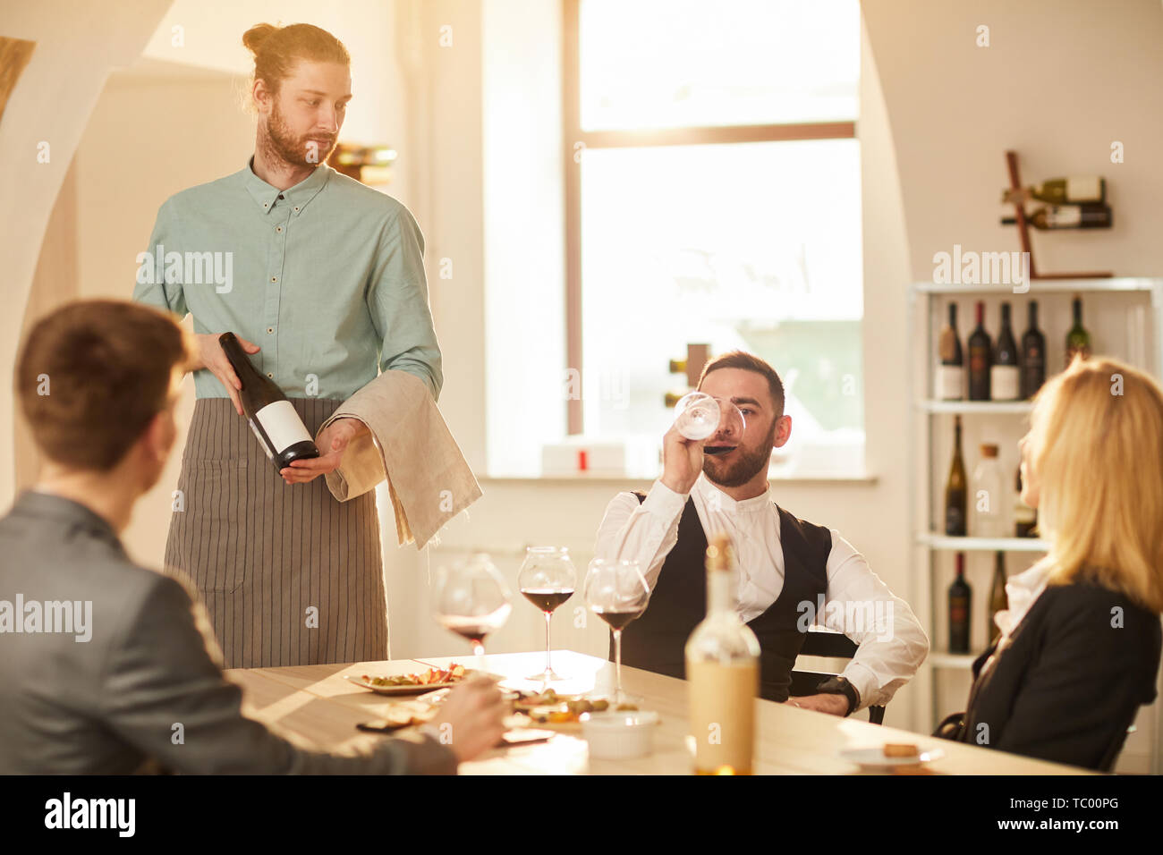 Portrait of waiter presenting bottle of wine at vineyard restaurant lit ...