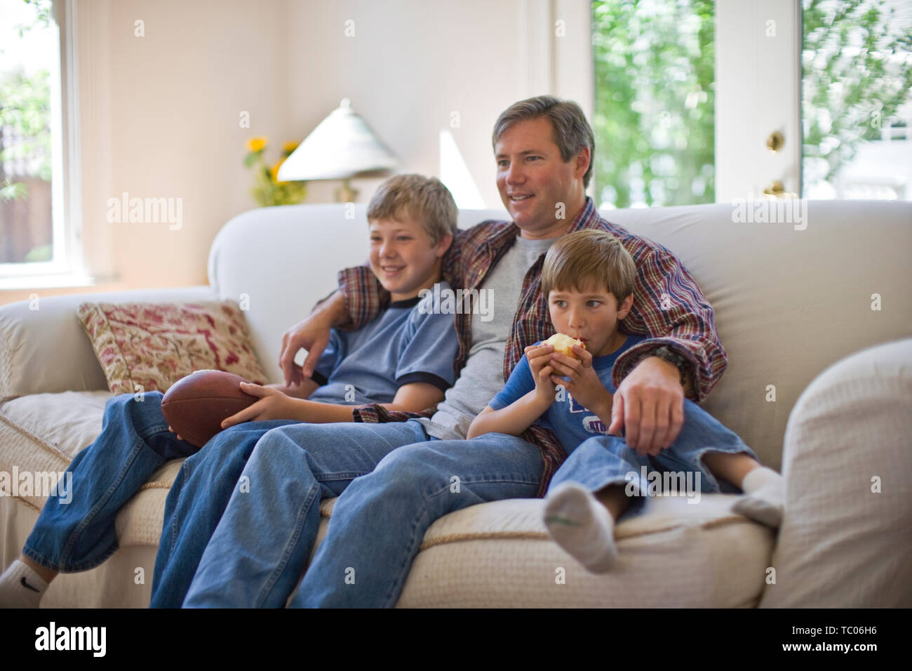 Mid-adult man sitting with an arm around his two young sons on a sofa ...
