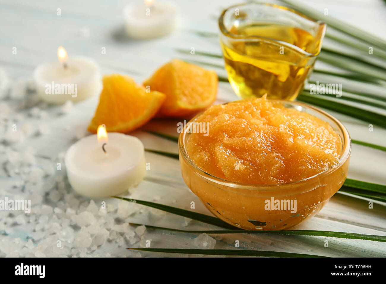 Bowl with orange body scrub, candles and essential oil on white wooden ...