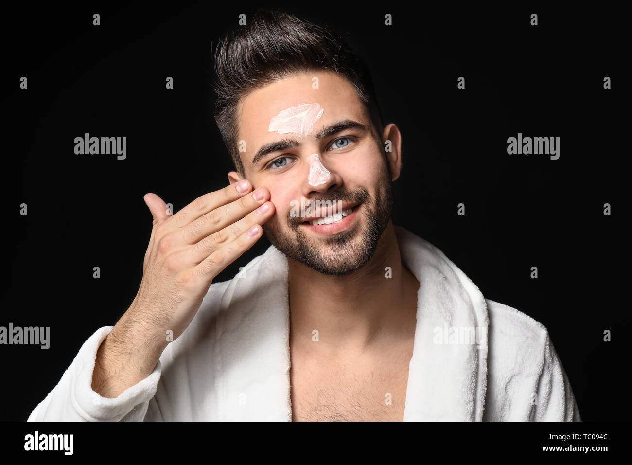 Handsome man applying clay mask on his face against dark background ...