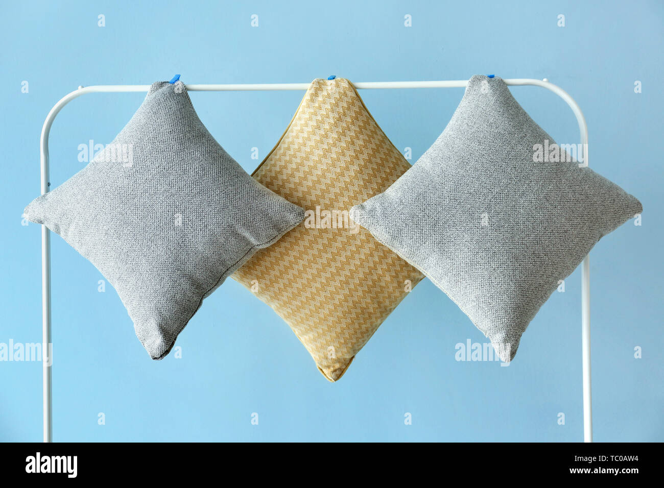 Soft pillows hanging on rack against color wall Stock Photo - Alamy