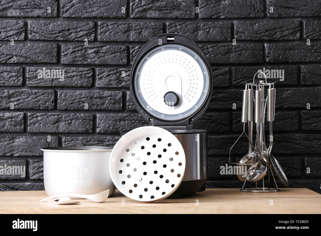 Modern multi cooker with accessories on table against dark background ...