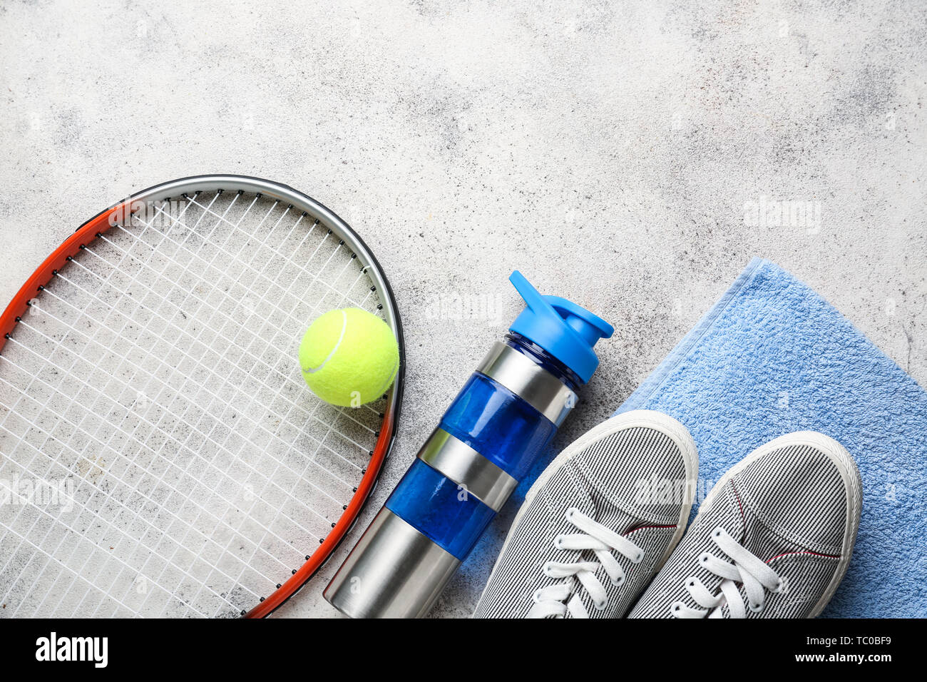 Tennis racket, shoes, bottle of water, towel and ball on grey ...