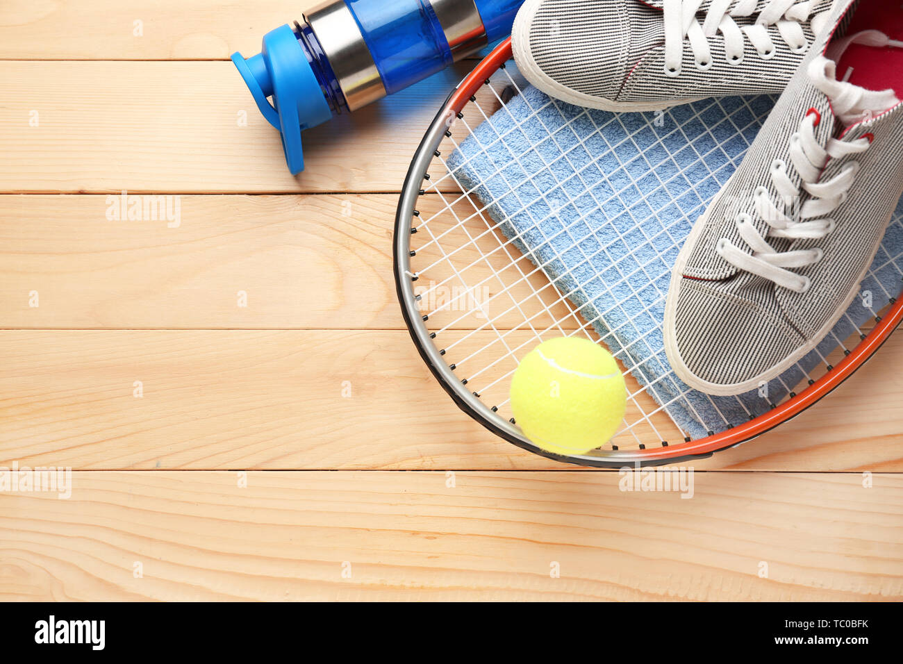 Tennis racket, shoes, towel, bottle of water and ball on wooden ...