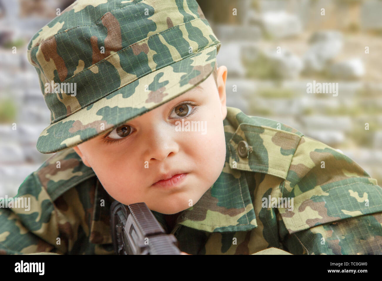 little Caucasian boy in military clothes and with toy weapons on the ...