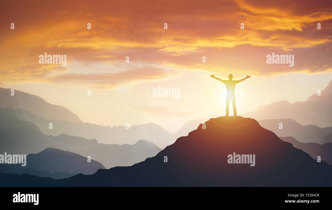 Man standing on edge of mountain feeling victorious with arms up in the ...
