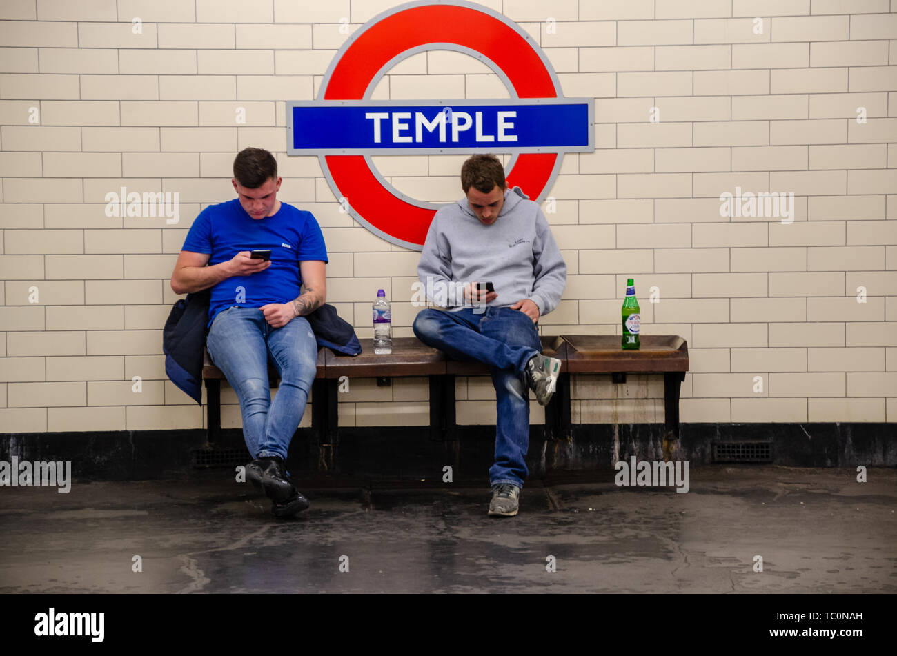 Two men sit on a bench on the platform at Temple London Underground ...