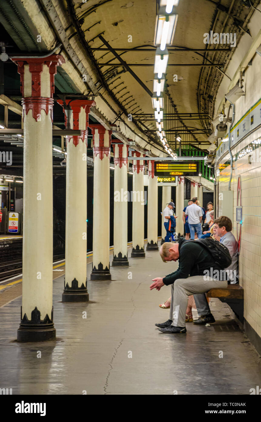 A man sits on a bench on the platform at Temple London Underground ...
