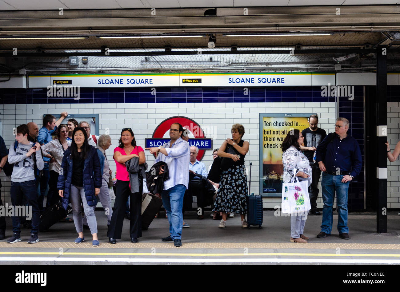 People stand and wait for a train on the platform at Sloane Square ...