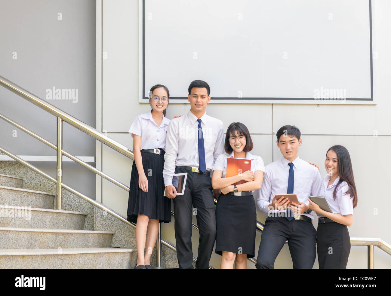 group of young students stand and smile on stairs with white billboard ...