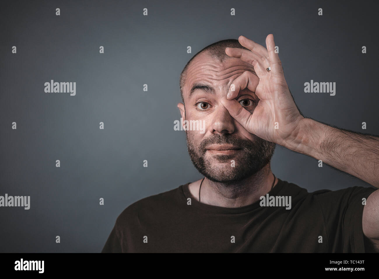 Portrait of a man looking through his fingers positioned to form a ...