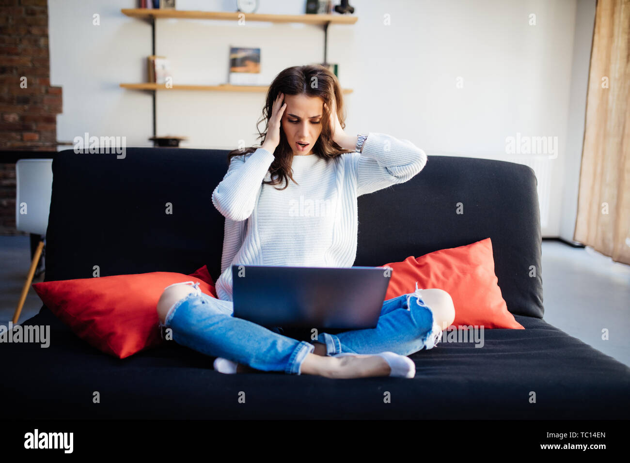 Shocked woman looking at laptop computer screen at home unpleasantly ...