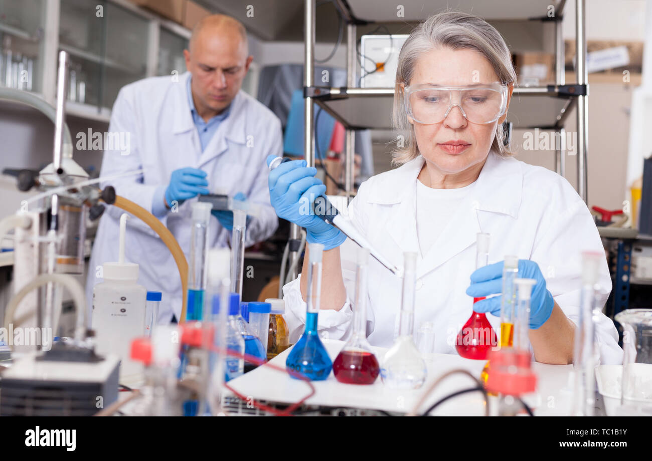 Experienced female biochemists mixing chemicals while performing ...