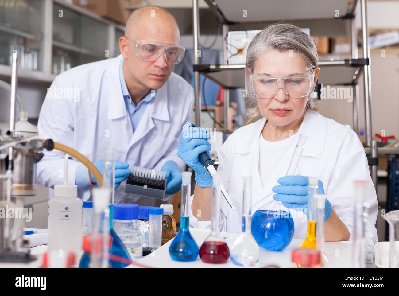 Two professional chemists working in laboratory, mixing reagents in ...