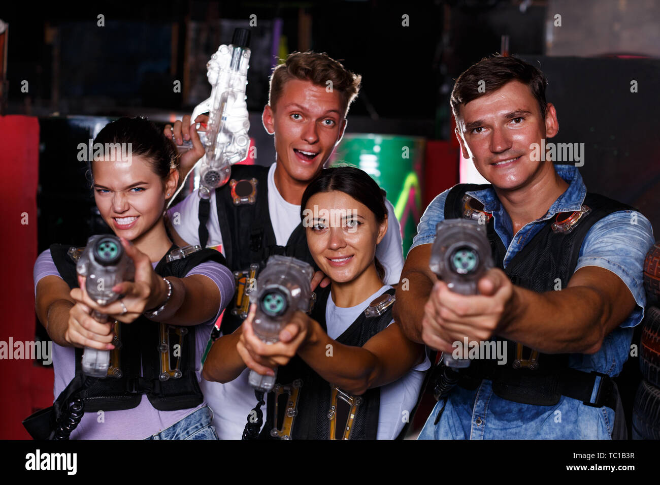 active friends standing with laser guns during laser tag game in dark ...