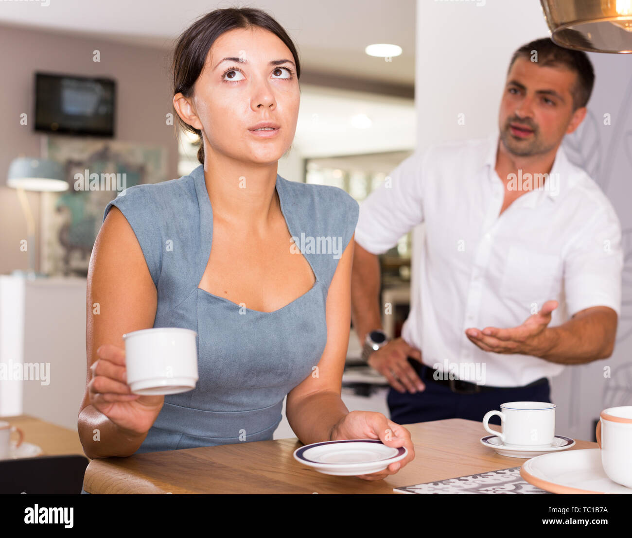 Upset young woman drinking tea at home table with disgruntled man ...