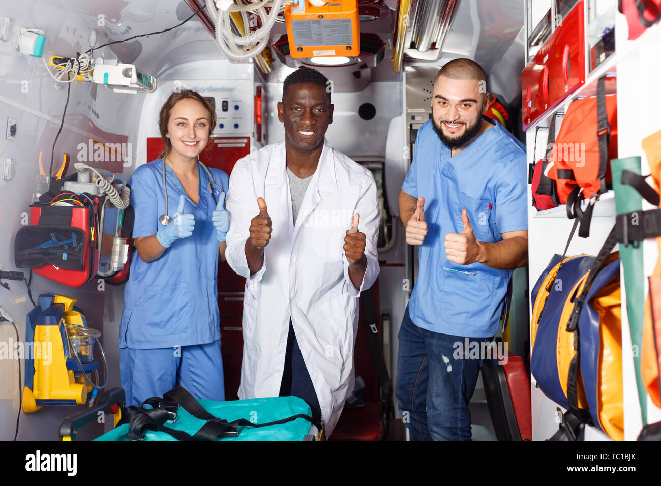 Three positive friendly efficient ambulance doctors posing in ambulance ...