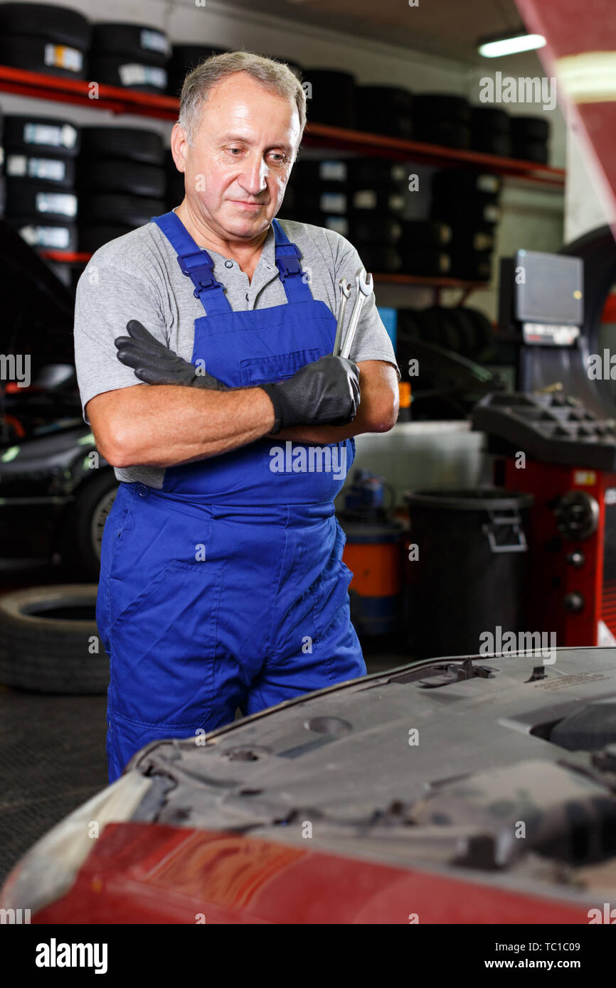 Pensive elderly man mechanic looking at car in auto workshop ...