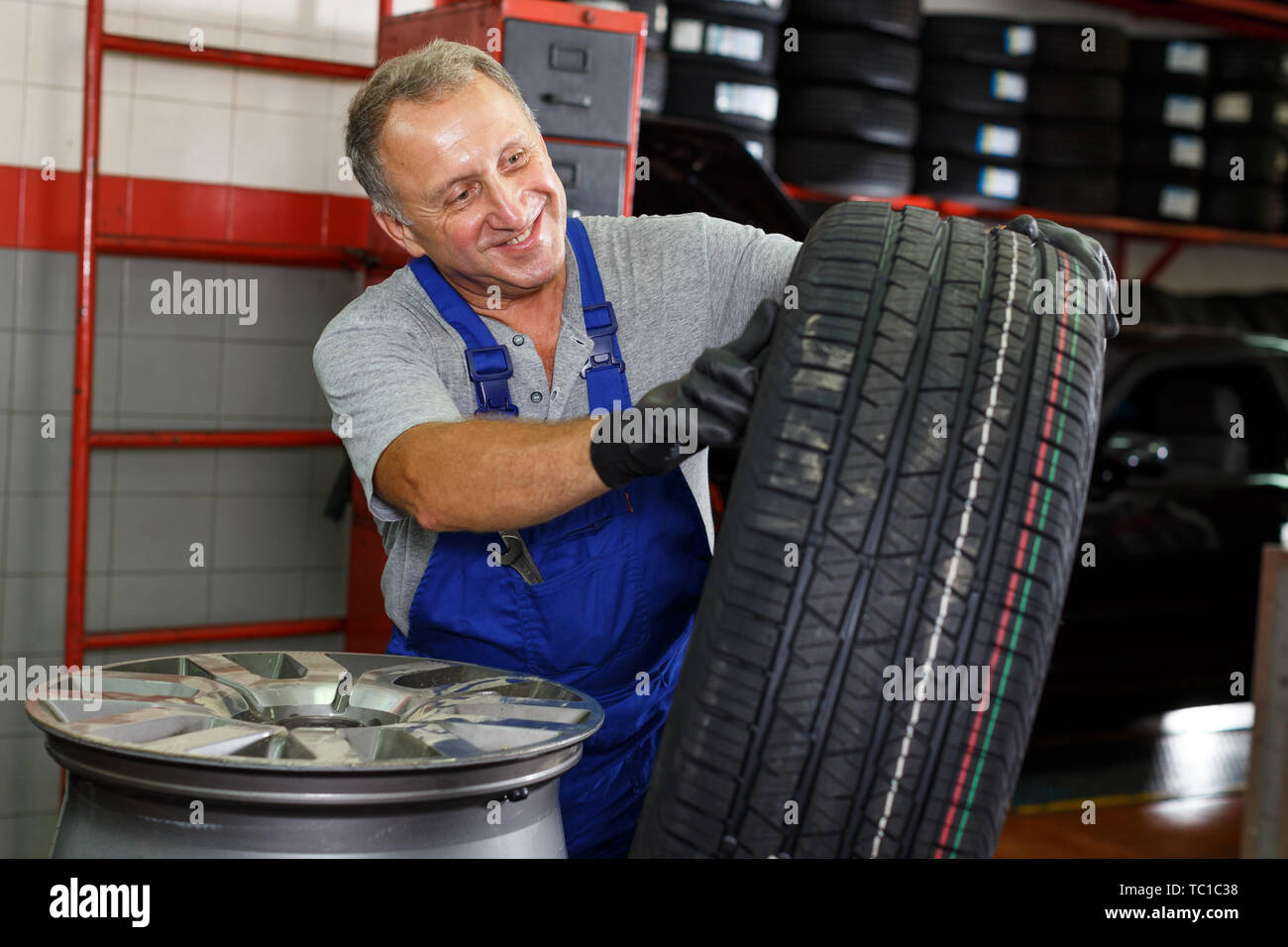 Mature man car mechanician removing tire from wheel disc in auto repair ...
