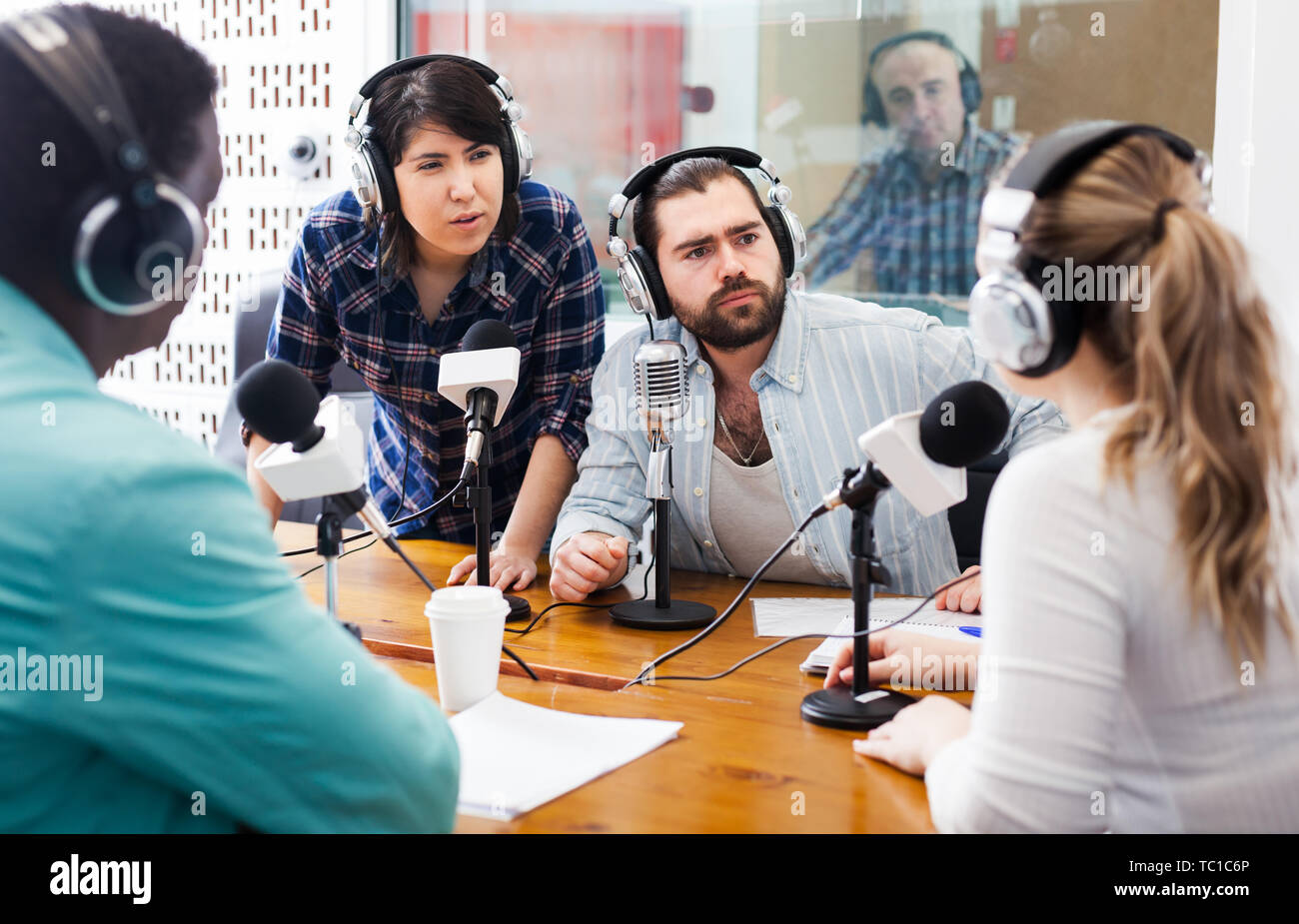 Smiling international team of radio presenters talking with guest in ...