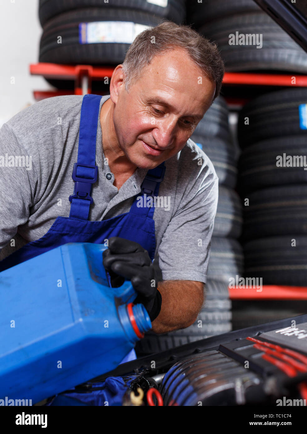 Elderly man mechanic engaged in replacement of engine oil in auto ...