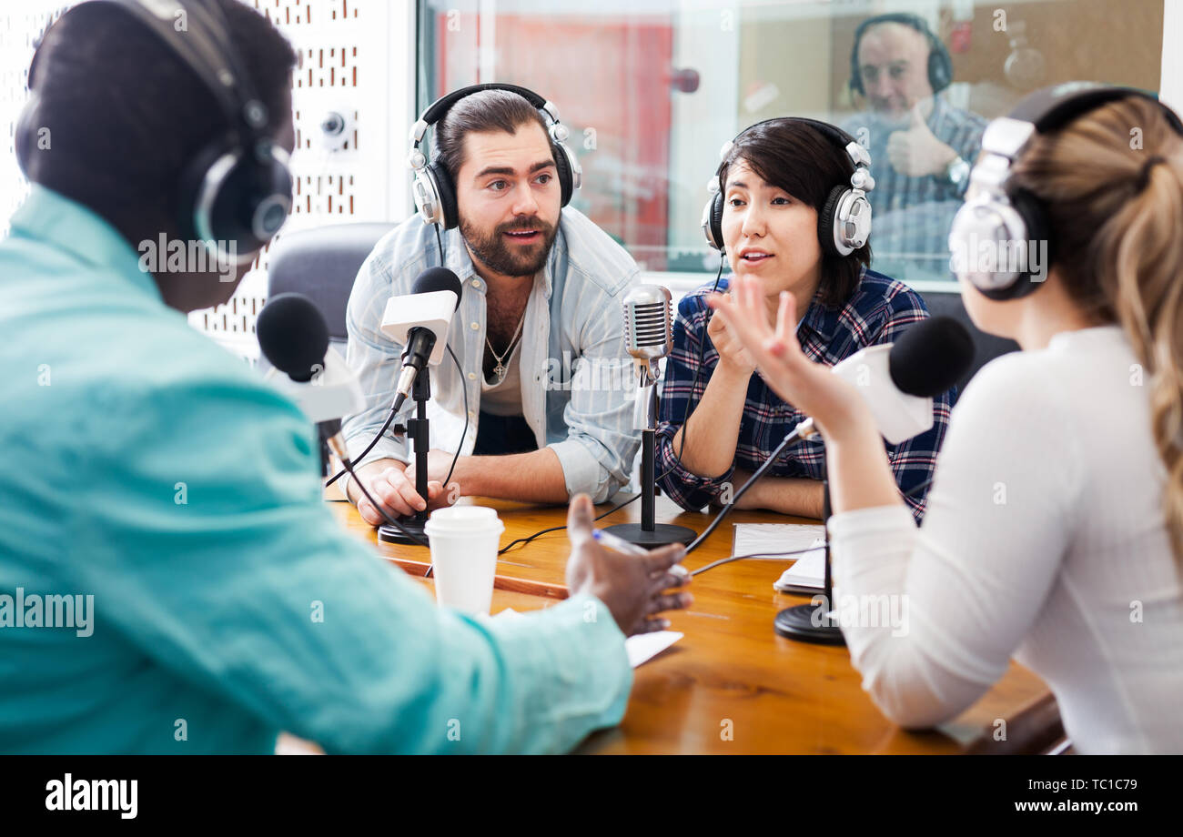 Smiling international team of radio hosts discussing with guest in ...