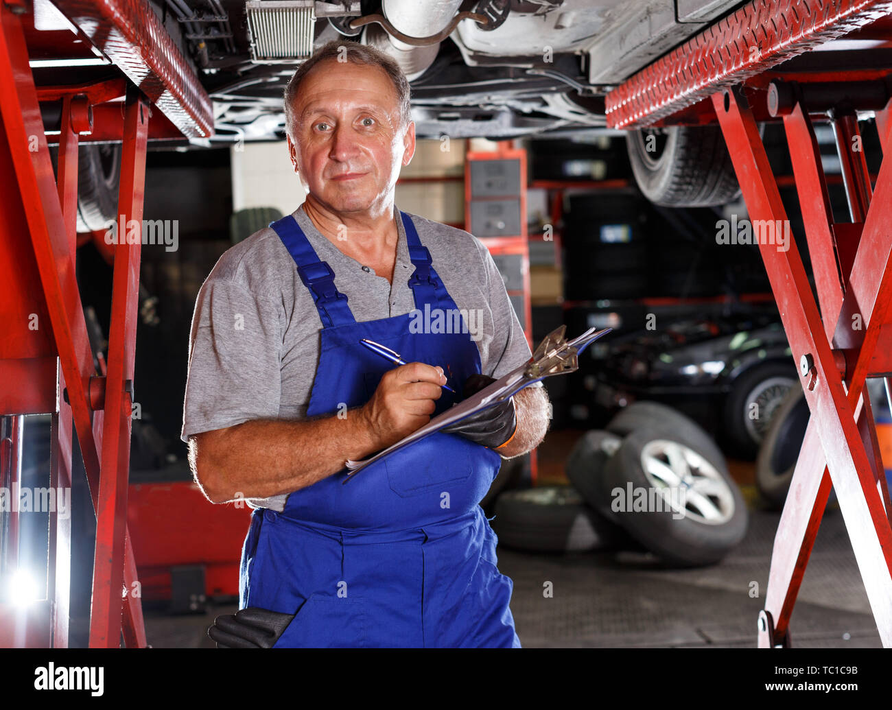 Confident male car mechanic in workshop writing job sheet for repairs ...