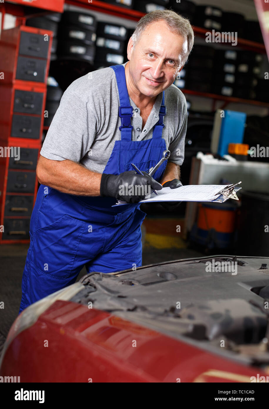 Confident male car mechanic in workshop writing job sheet for repairs ...