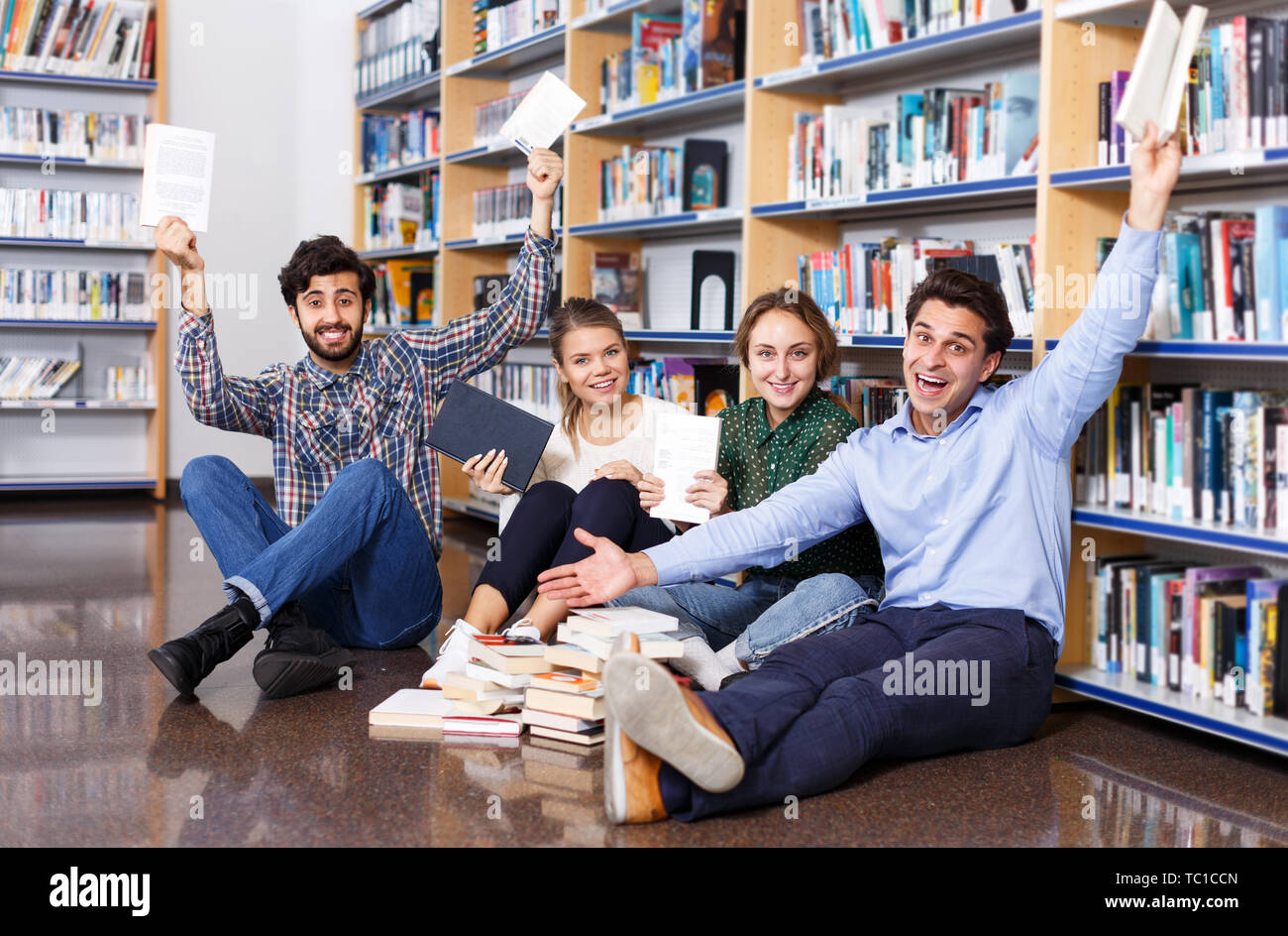 Cheerful group of university students reading textbooks together while ...