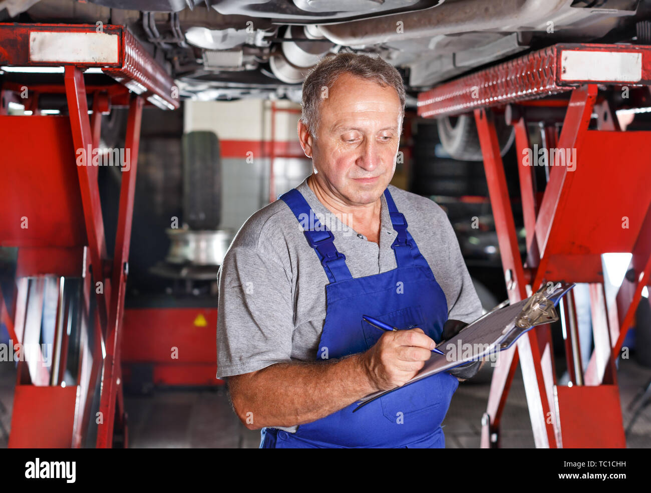 Confident male car mechanic at a workshop writing job sheet for repairs ...