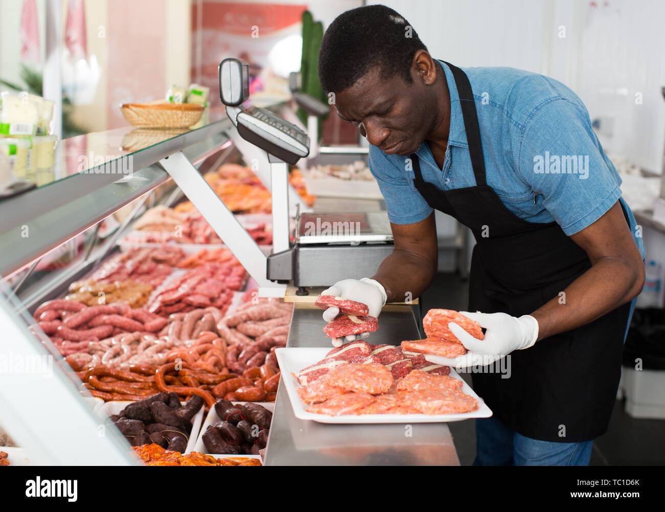 Professional butcher arranging meat products in display case of butcher ...