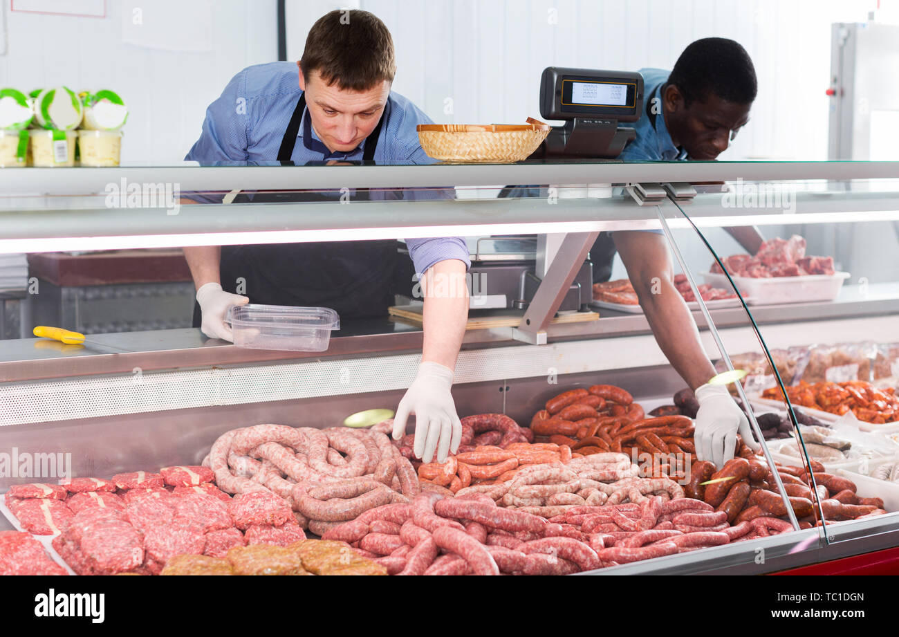 Skillful positive butcher with colleague working behind counter in ...