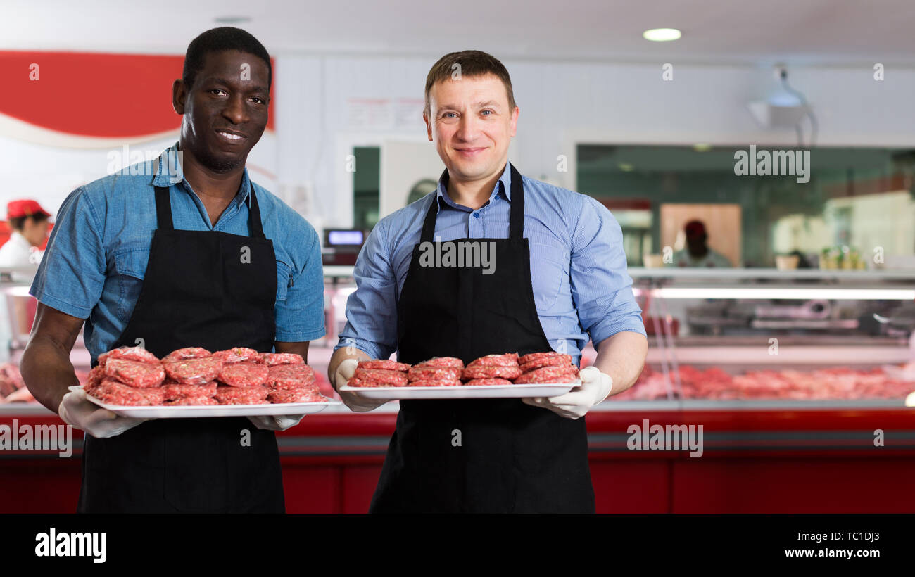 Two professional butchers standing in butcher shop with trays of fresh ...