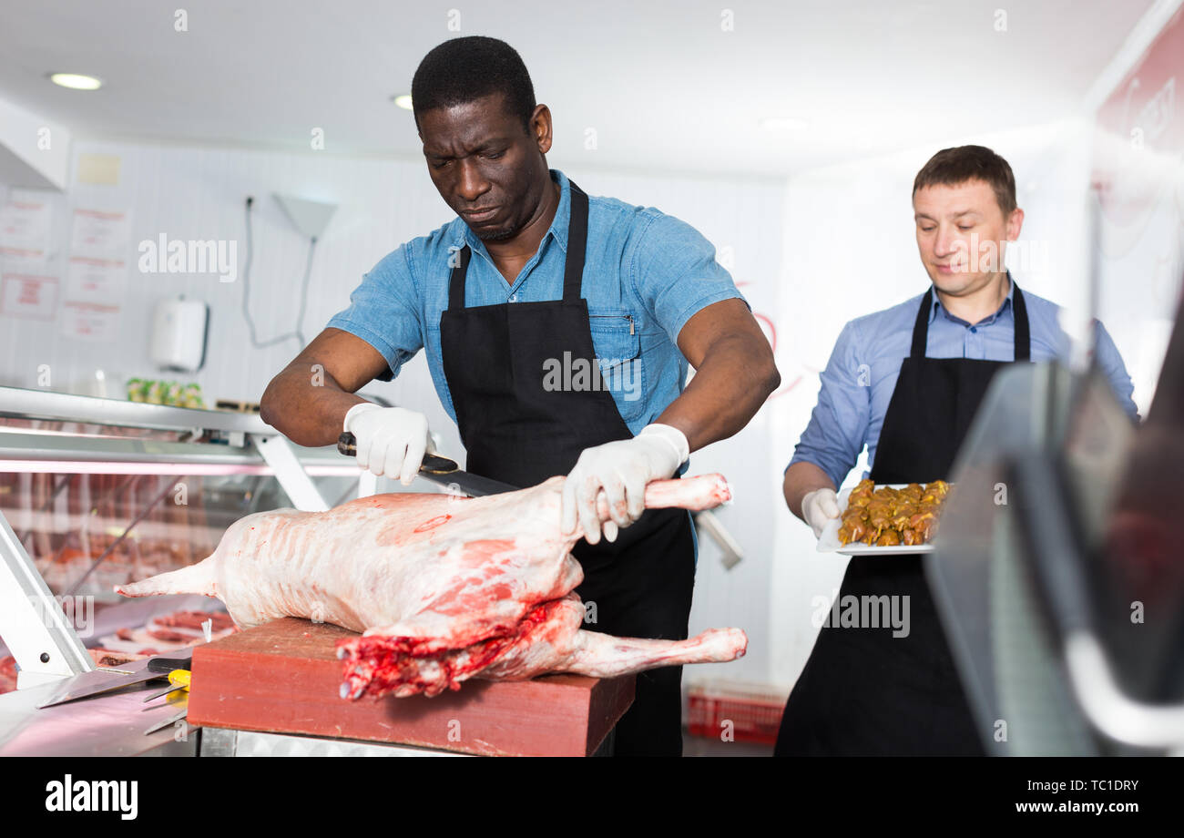 African American male butcher cutting lamb carcass in butcher shop ...