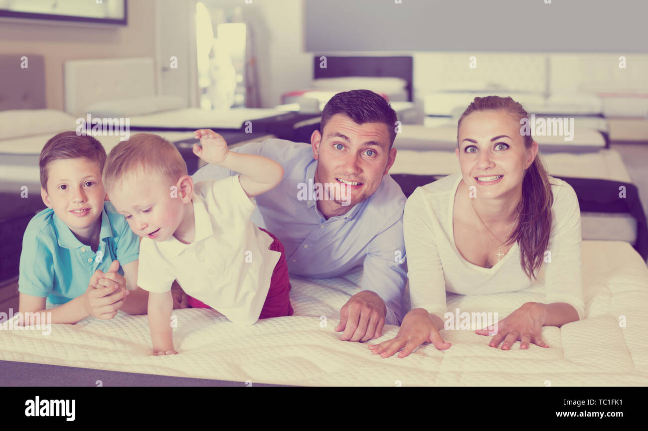 happy italian parents with two young sons testing mattress in store ...