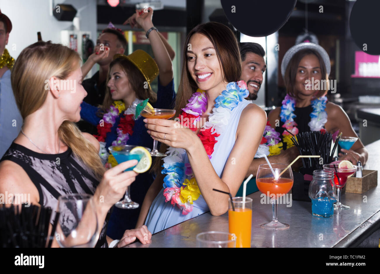 Two young smiling women in lei are drinking cocktails on hawaiian party ...