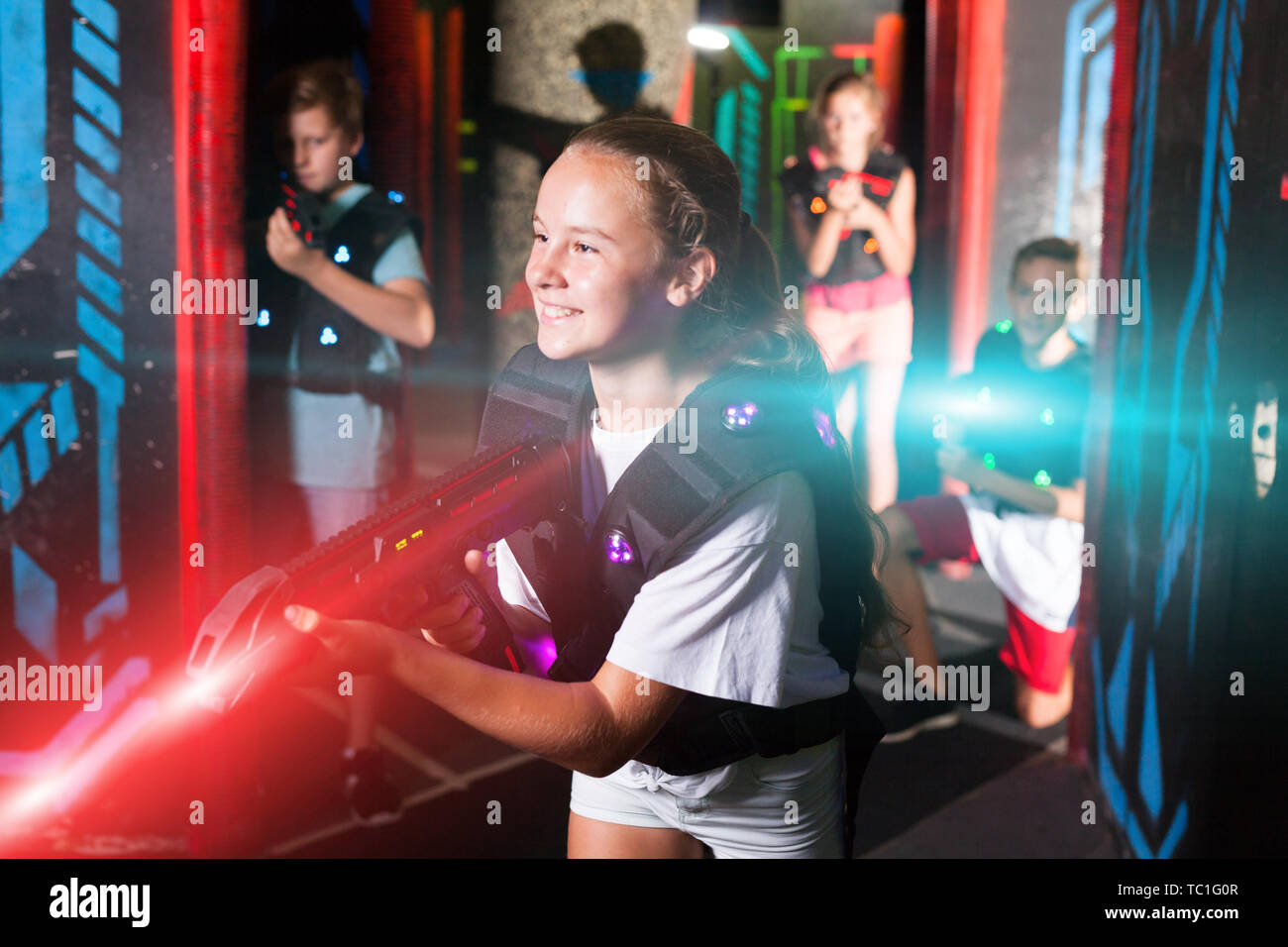 Emotional teen girl with laser pistol playing laser tag with friends on ...