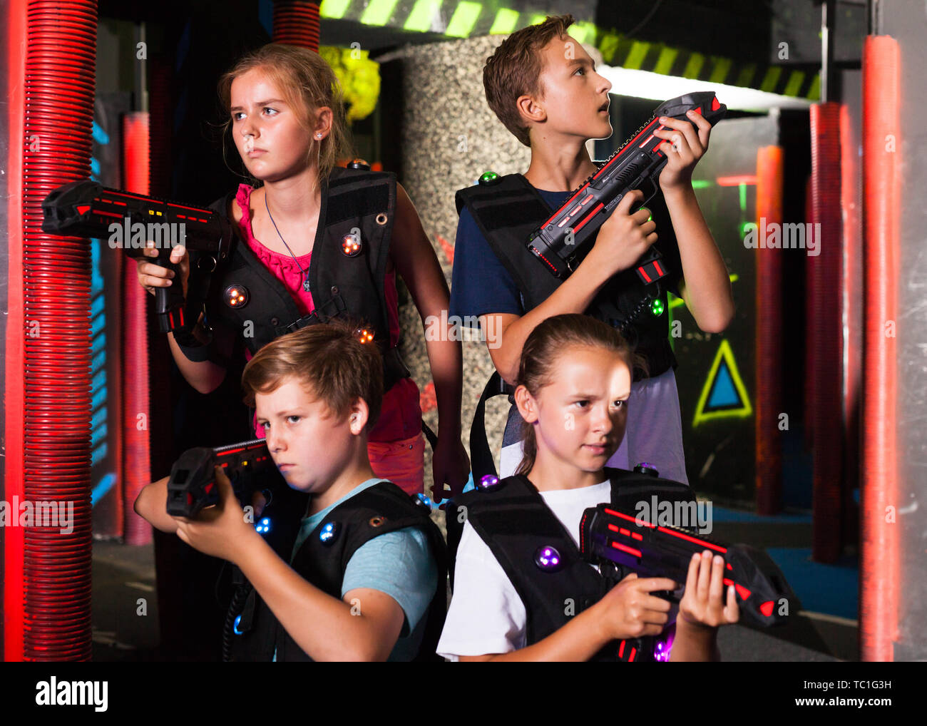 Cheerful teen girls and boys with laser pistols posing together in dark ...