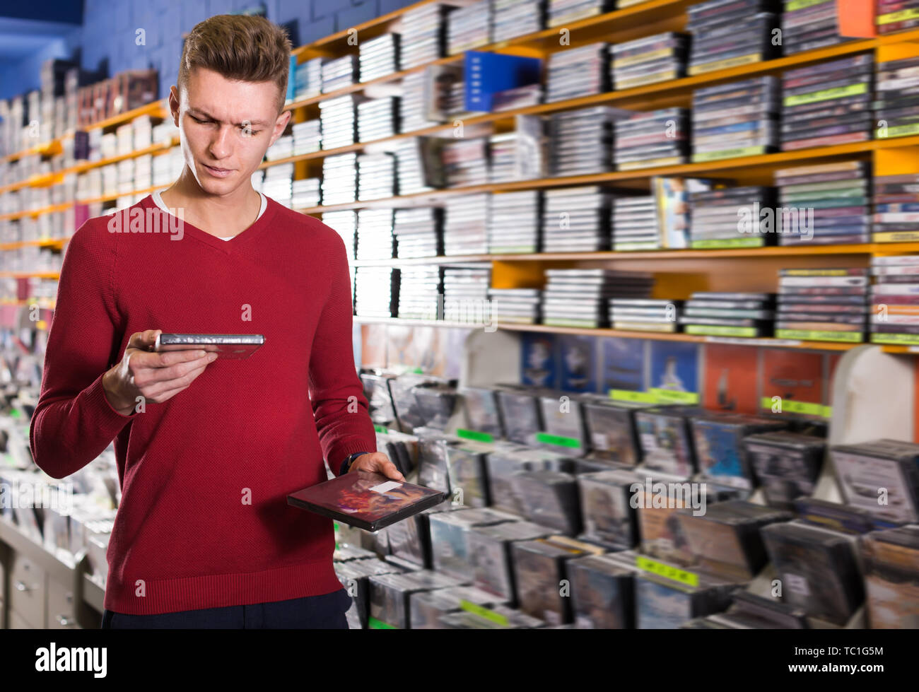 Adult guy looking for interesting movies on shelves of CD shop Stock ...