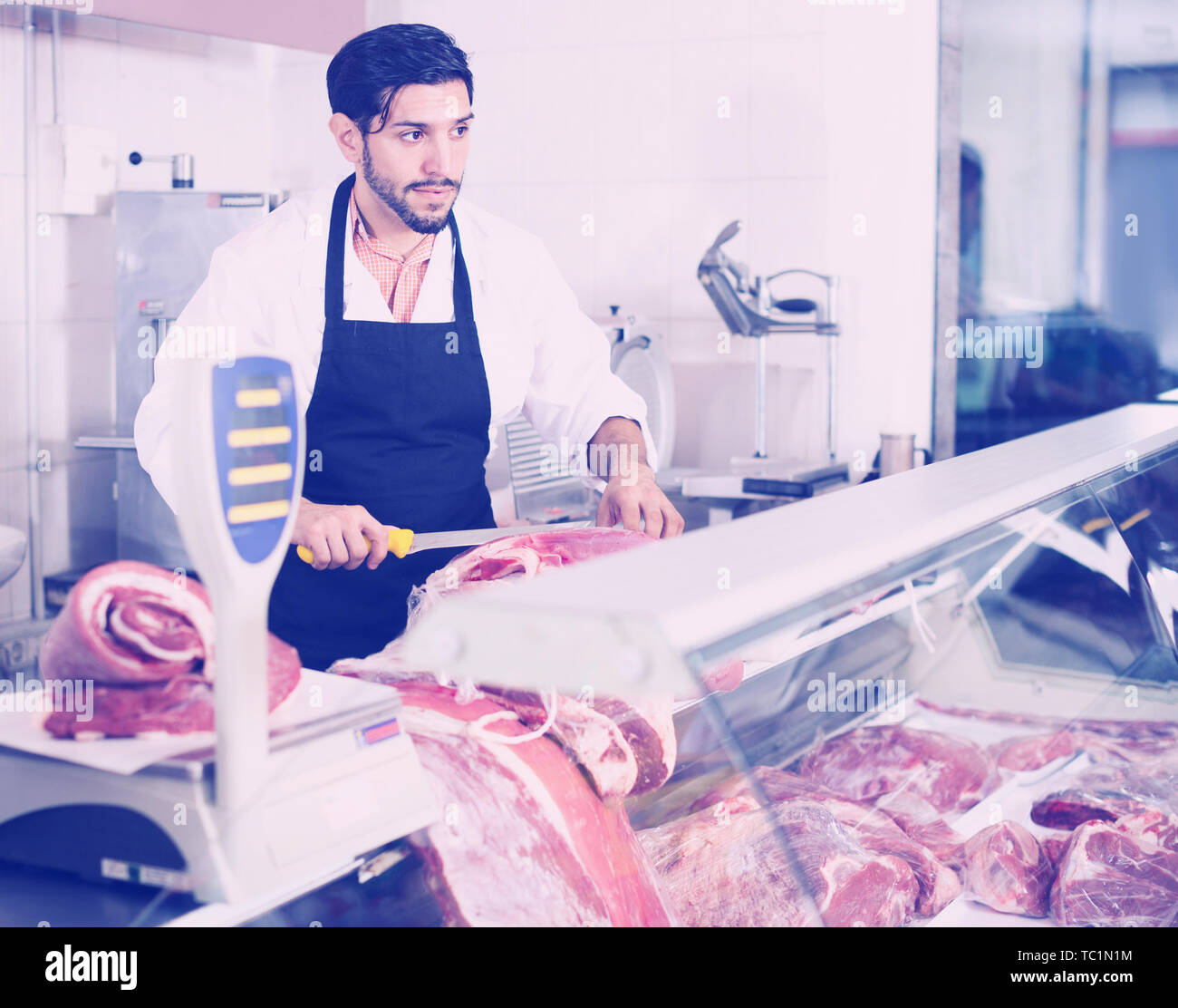 Adult man butcher cutting fresh meat for client in food shop Stock ...