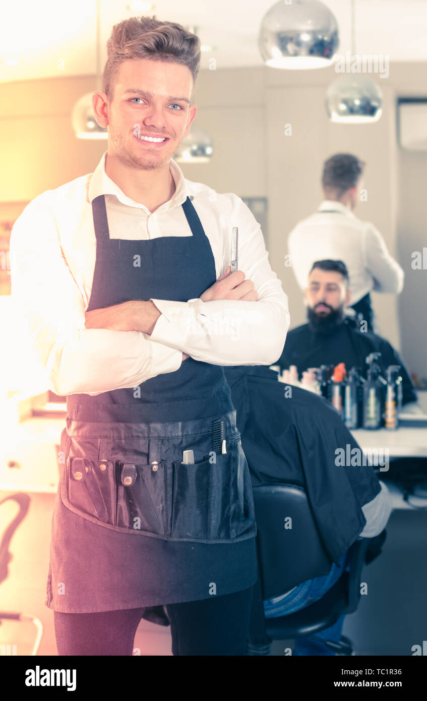 Young guy displaying his workplace and tools at hairdressing salon ...
