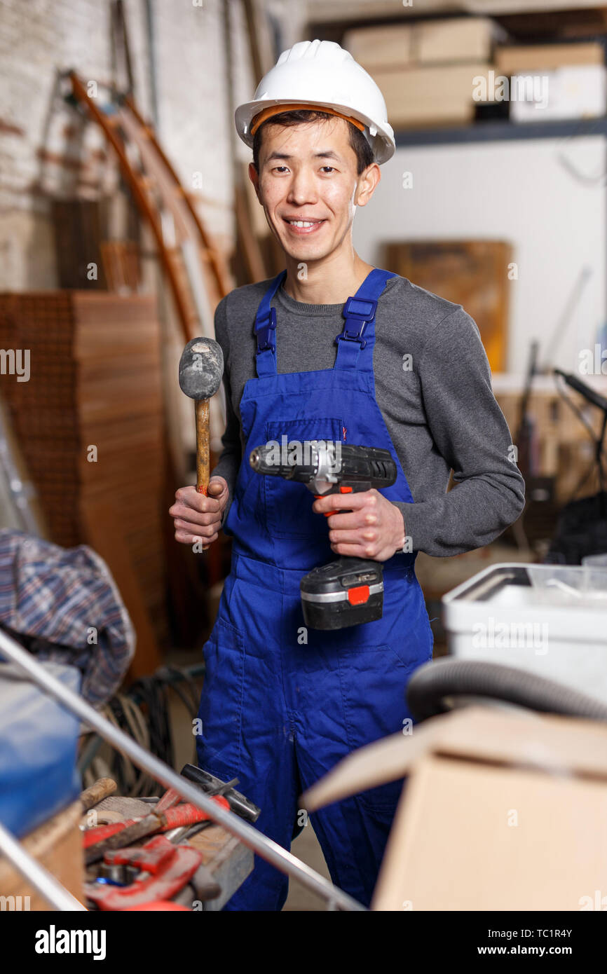 Asian worker in work wear holding power tools inside built cottage ...