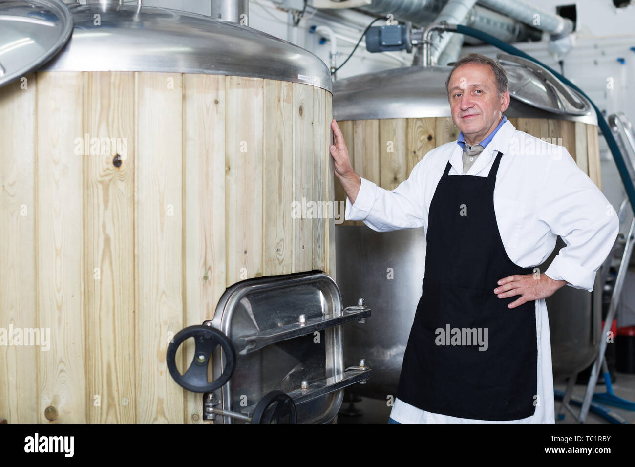 Brewer is standing near reservoir for beer on his workplace indoor ...