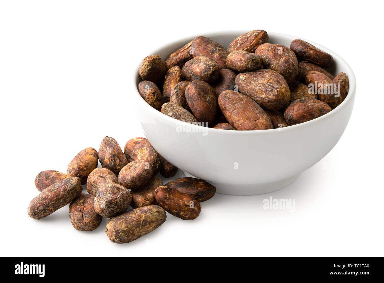 Roasted unpeeled cocoa beans in a white ceramic bowl next to a pile of ...