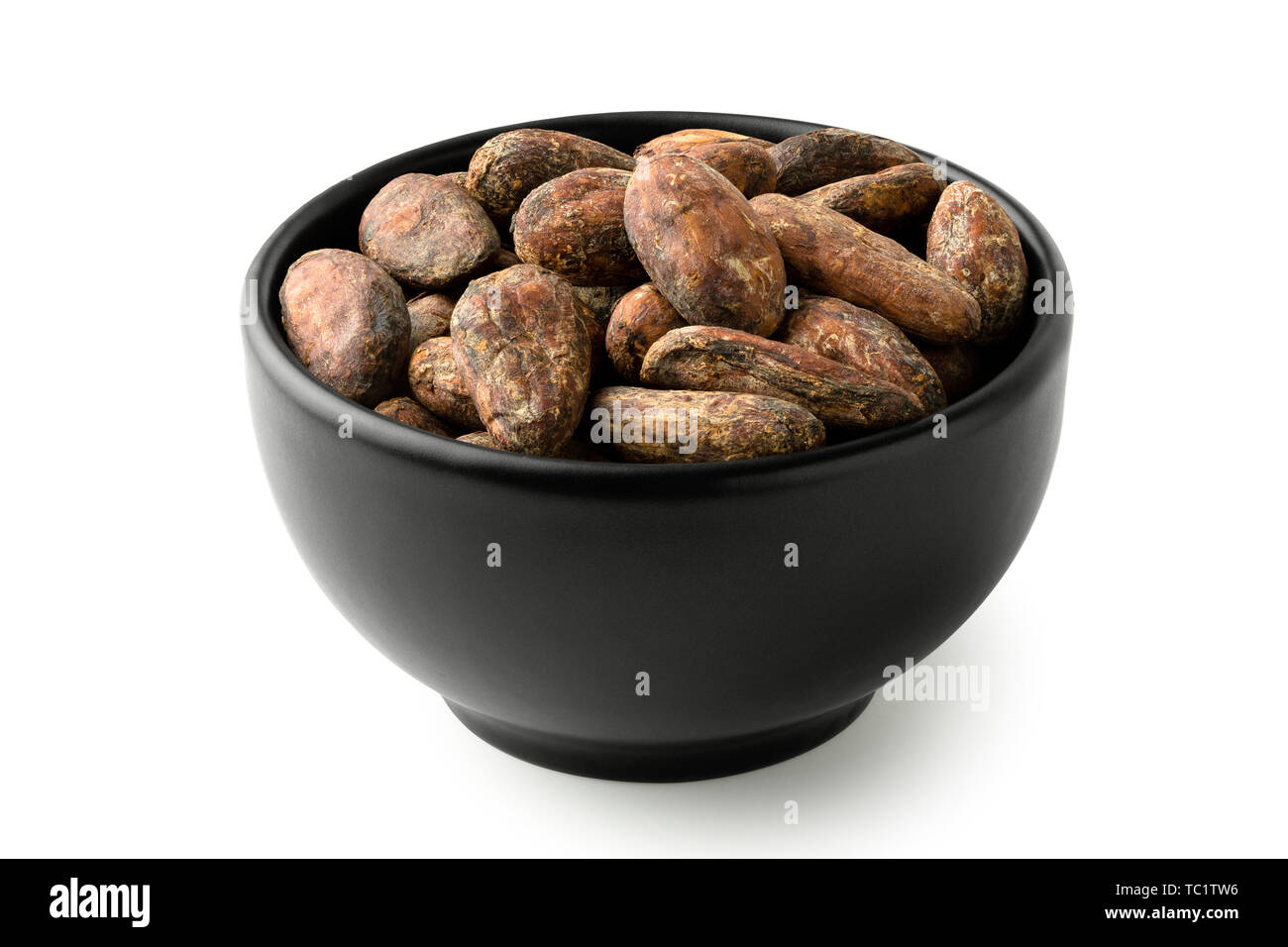 Roasted unpeeled cocoa beans in a black ceramic bowl isolated on white ...