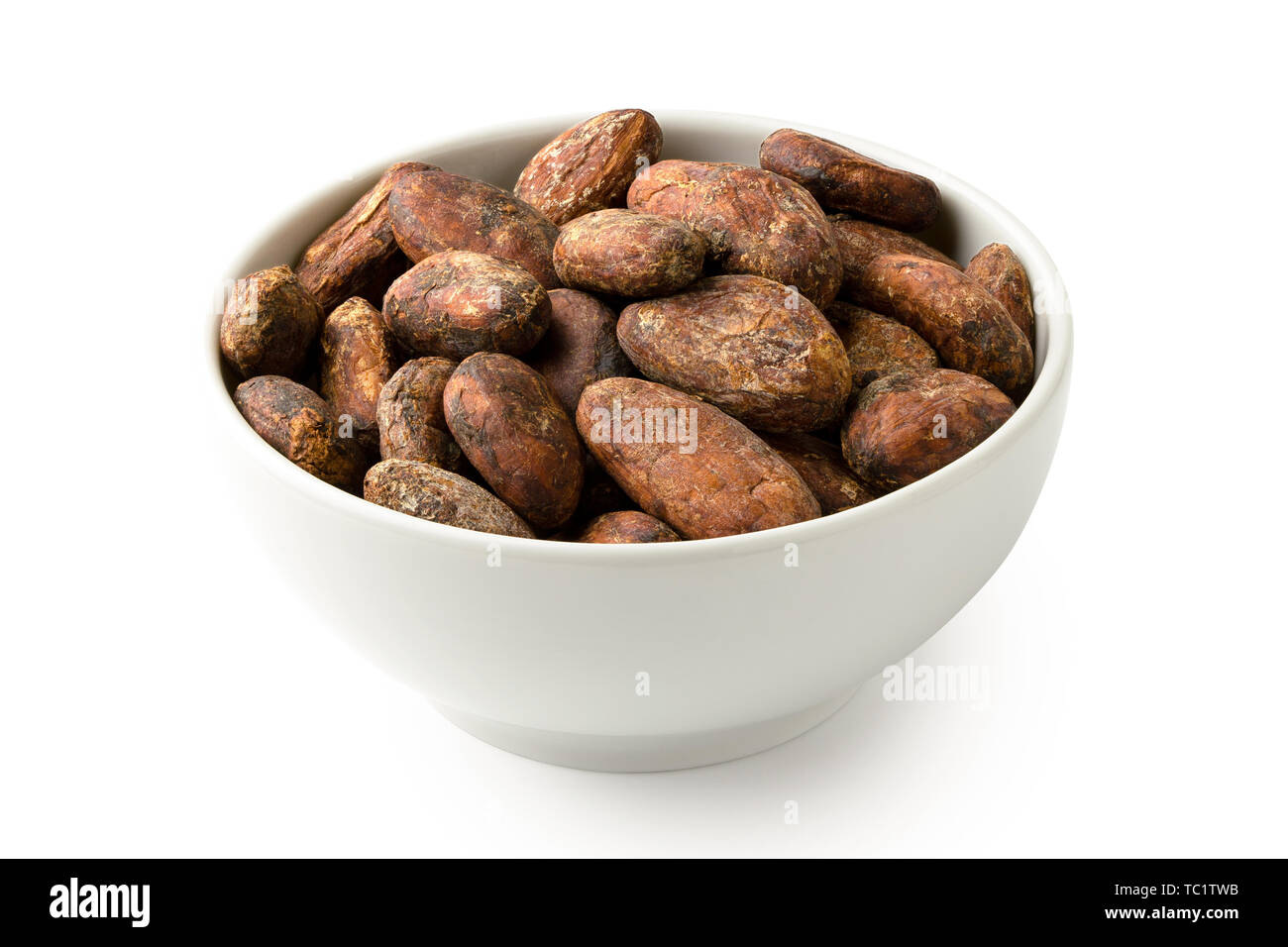 Roasted unpeeled cocoa beans in a white ceramic bowl isolated on white ...