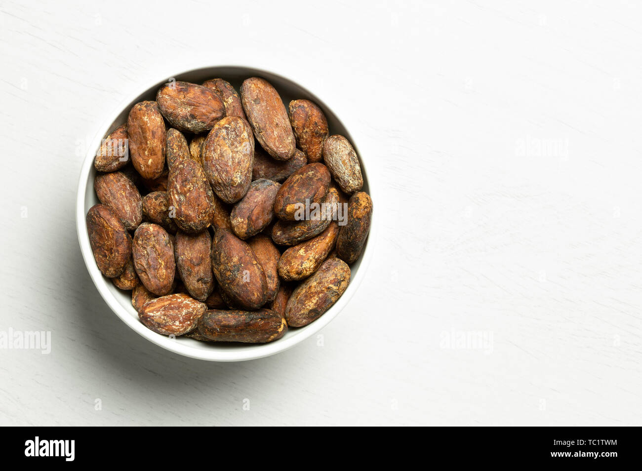 Roasted unpeeled cocoa beans in a white ceramic bowl isolated on white ...